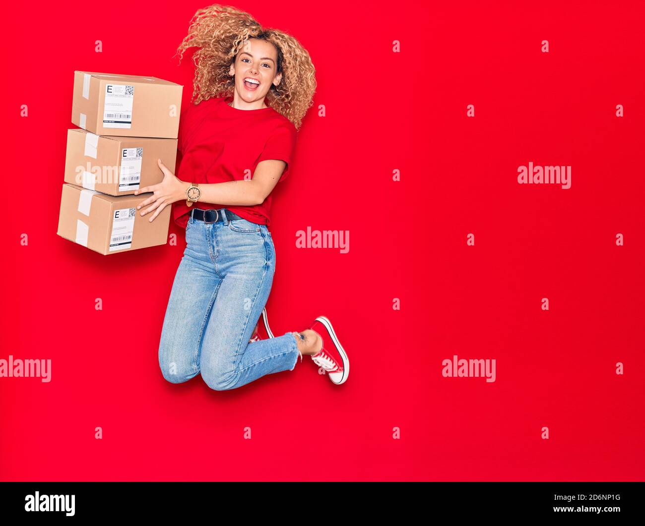 Young beautiful curly deliverywoman holding package smiling happy ...