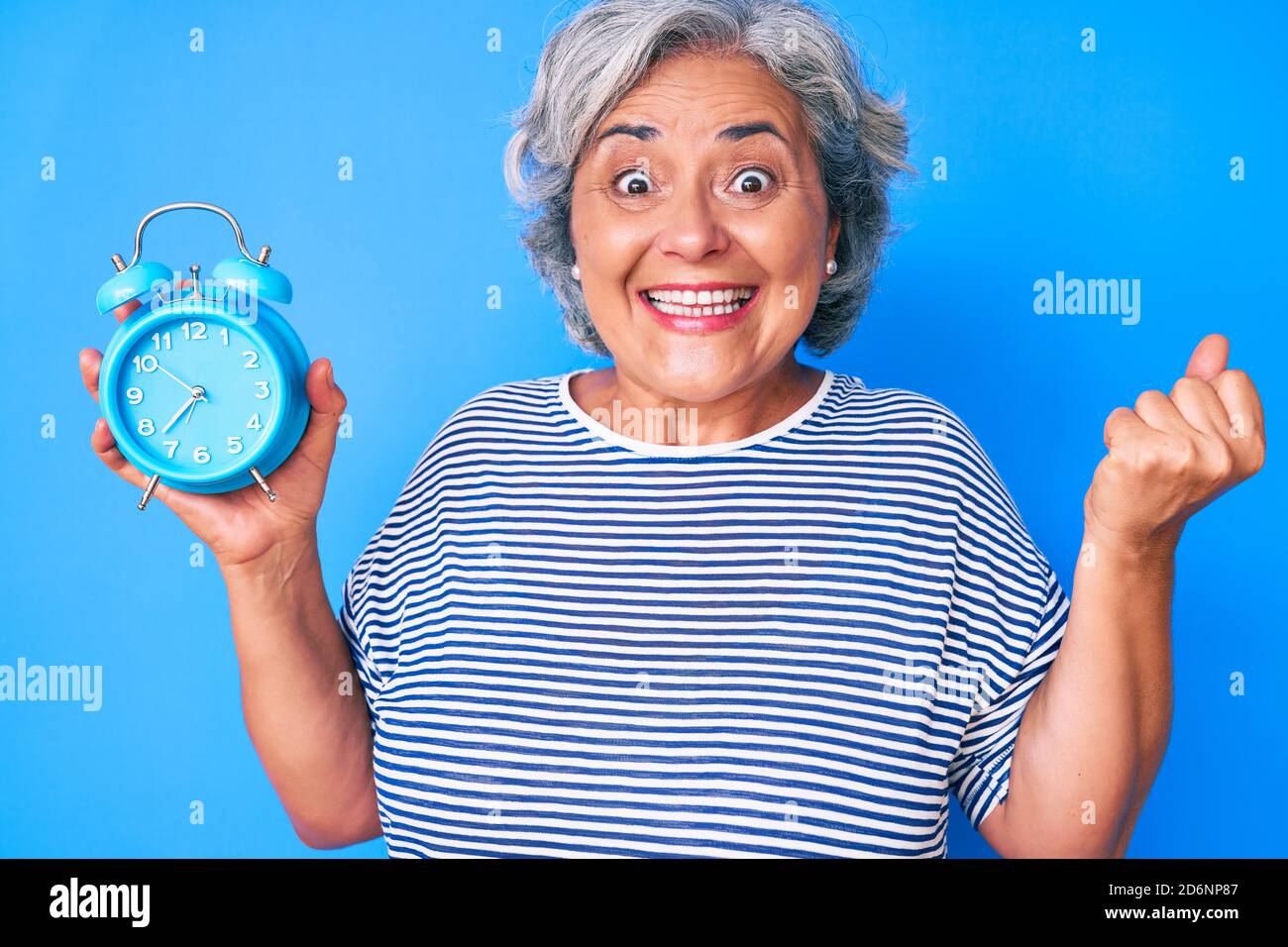 Senior hispanic woman holding alarm clock screaming proud, celebrating ...