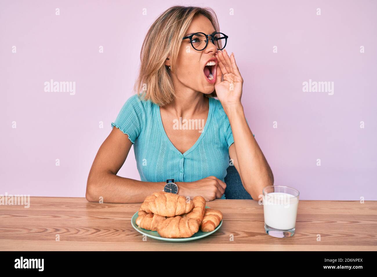 Beautiful caucasian woman eating croissant for breakfast shouting and ...