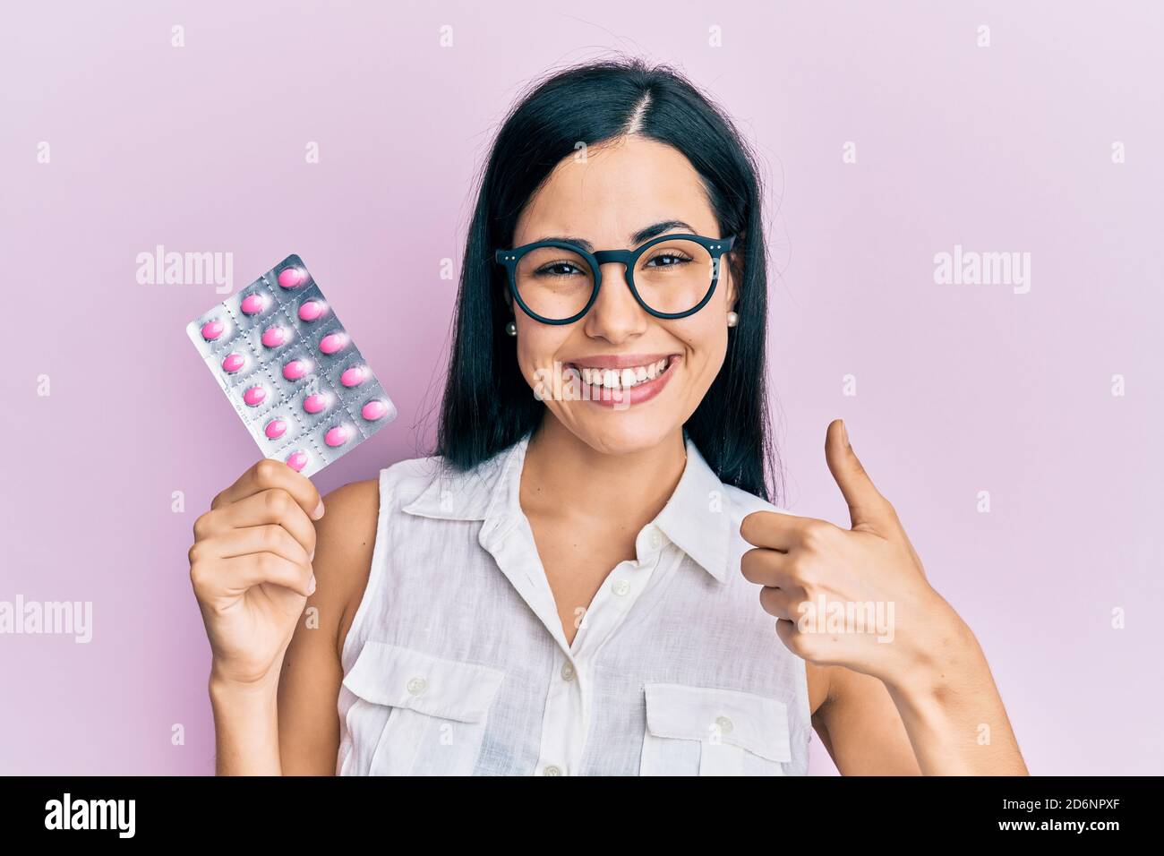 Beautiful young woman holding pills smiling happy and positive, thumb ...