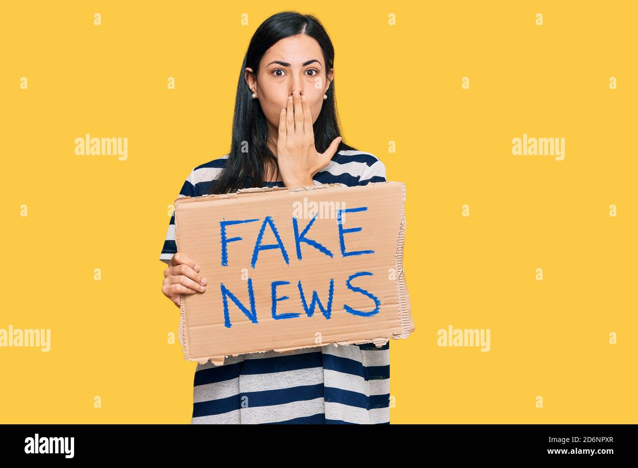 Beautiful young woman holding fake news banner covering mouth with hand ...