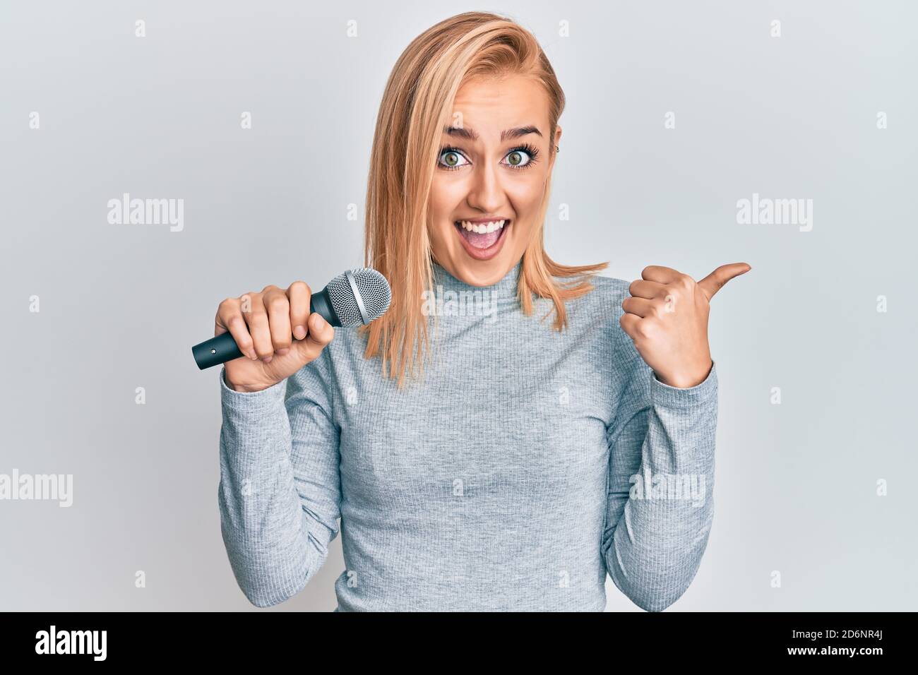 Beautiful caucasian woman singing song using microphone pointing thumb ...