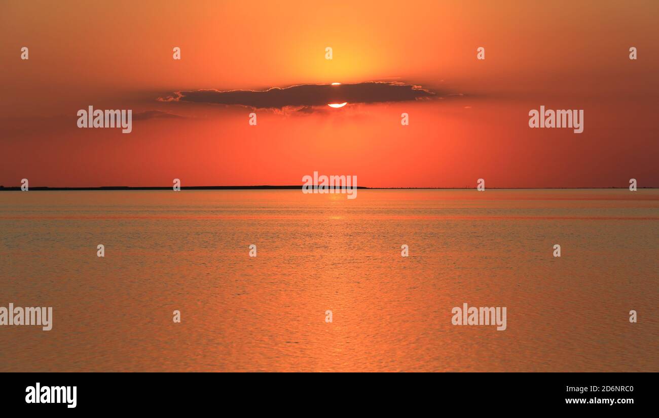 Red sunset landscape with sun behind clouds over sea Stock Photo - Alamy