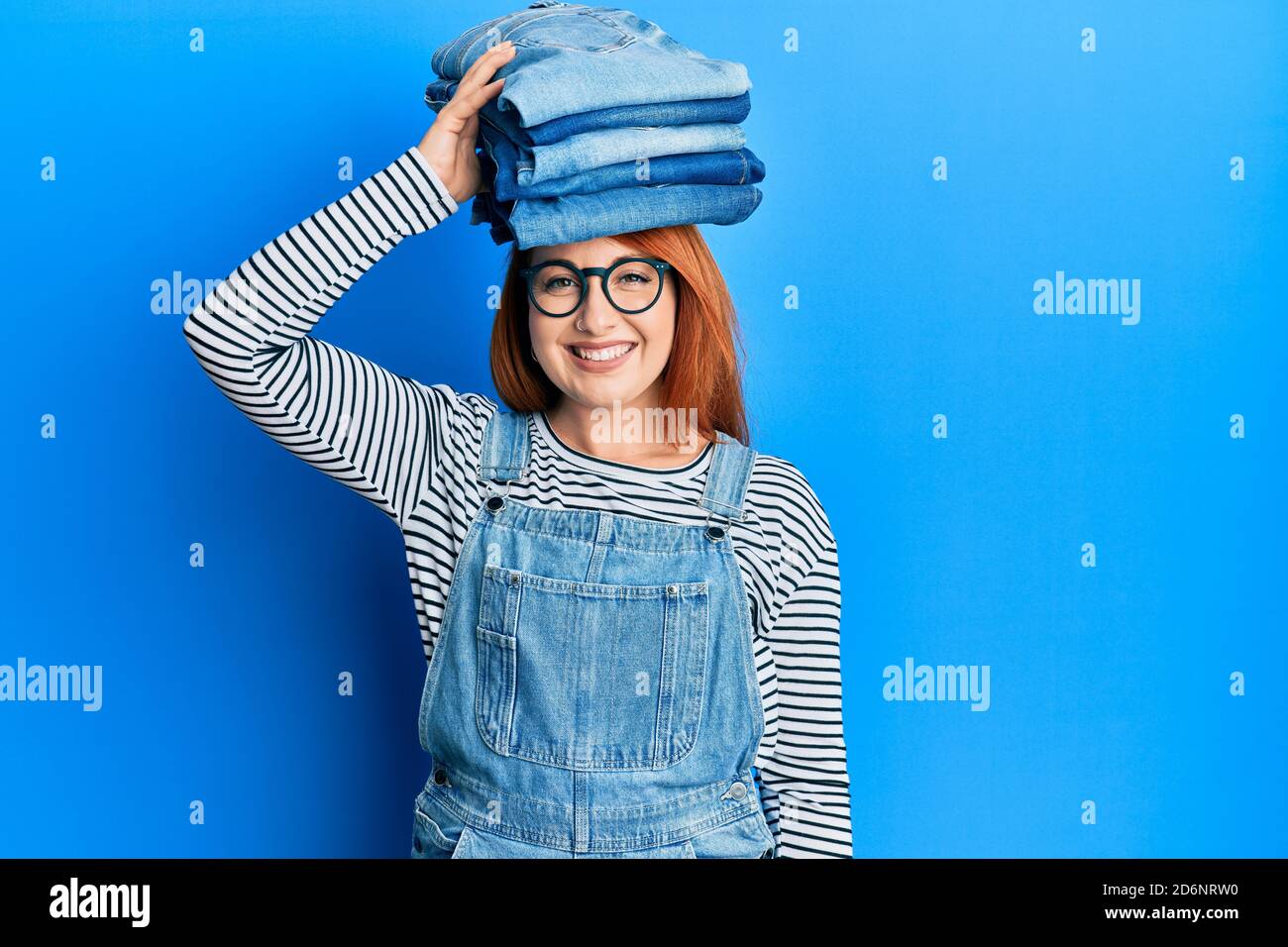 Beautiful redhead woman holding stack of folded jeans over head looking ...