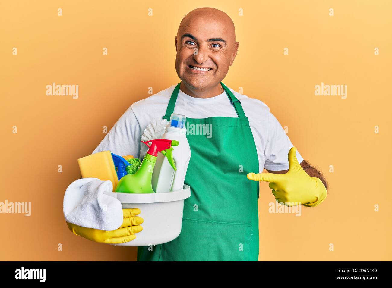 Mature middle east man wearing cleaner apron holding cleaning products ...
