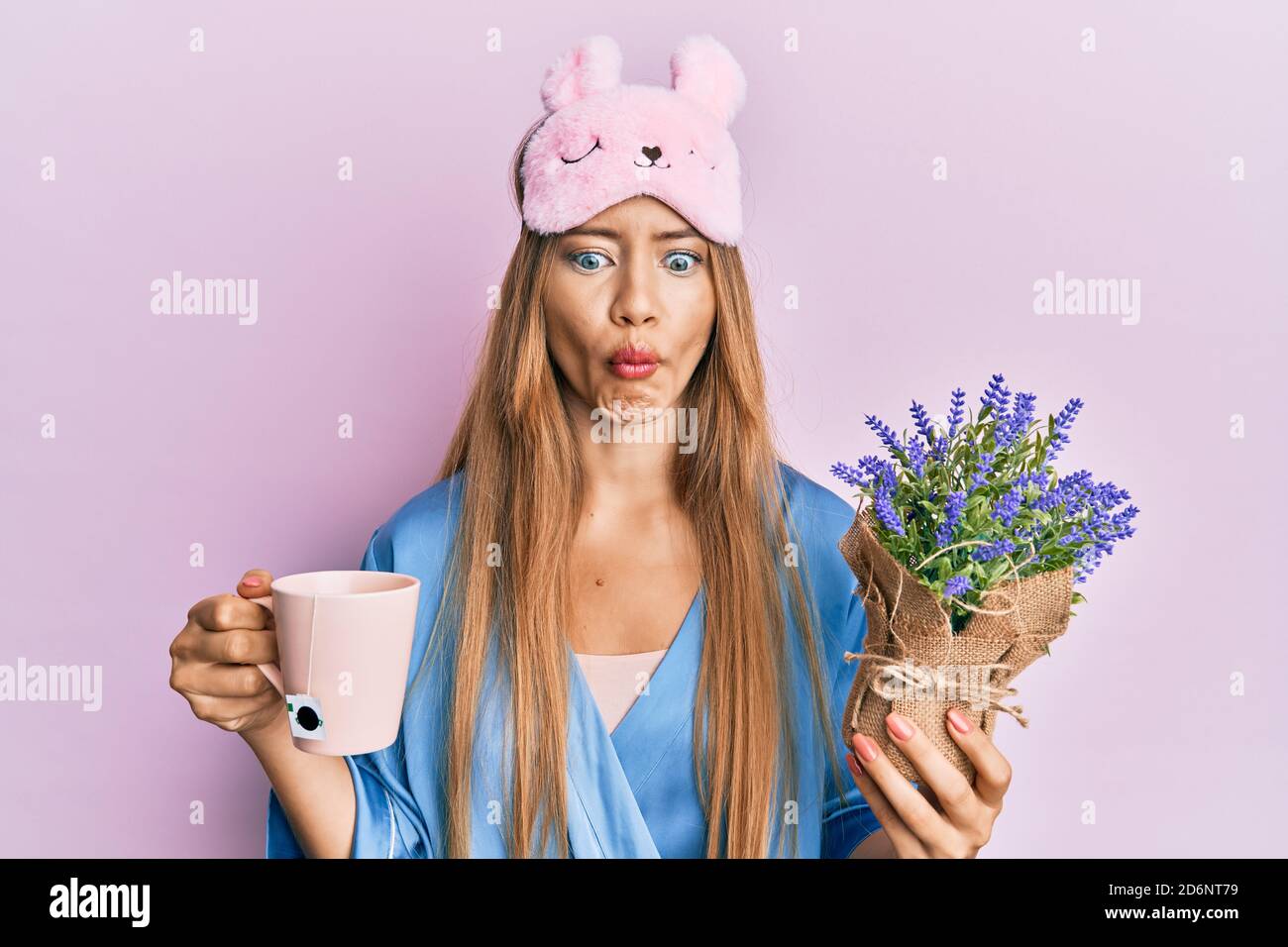 Beautiful young blonde woman wearing pajama drinking a cup of infused ...