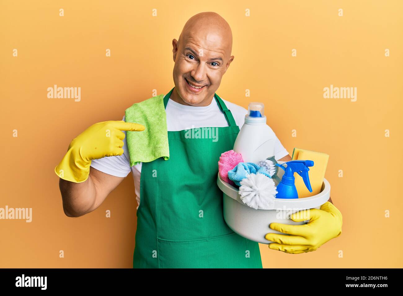 Middle age bald man wearing cleaner apron holding cleaning products ...