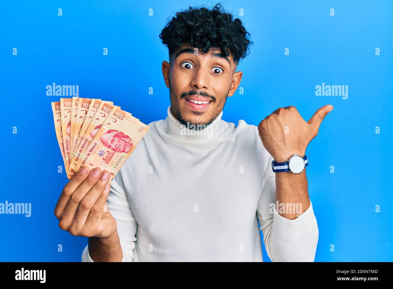 Young arab handsome man holding 100 mexican pesos banknotes pointing ...