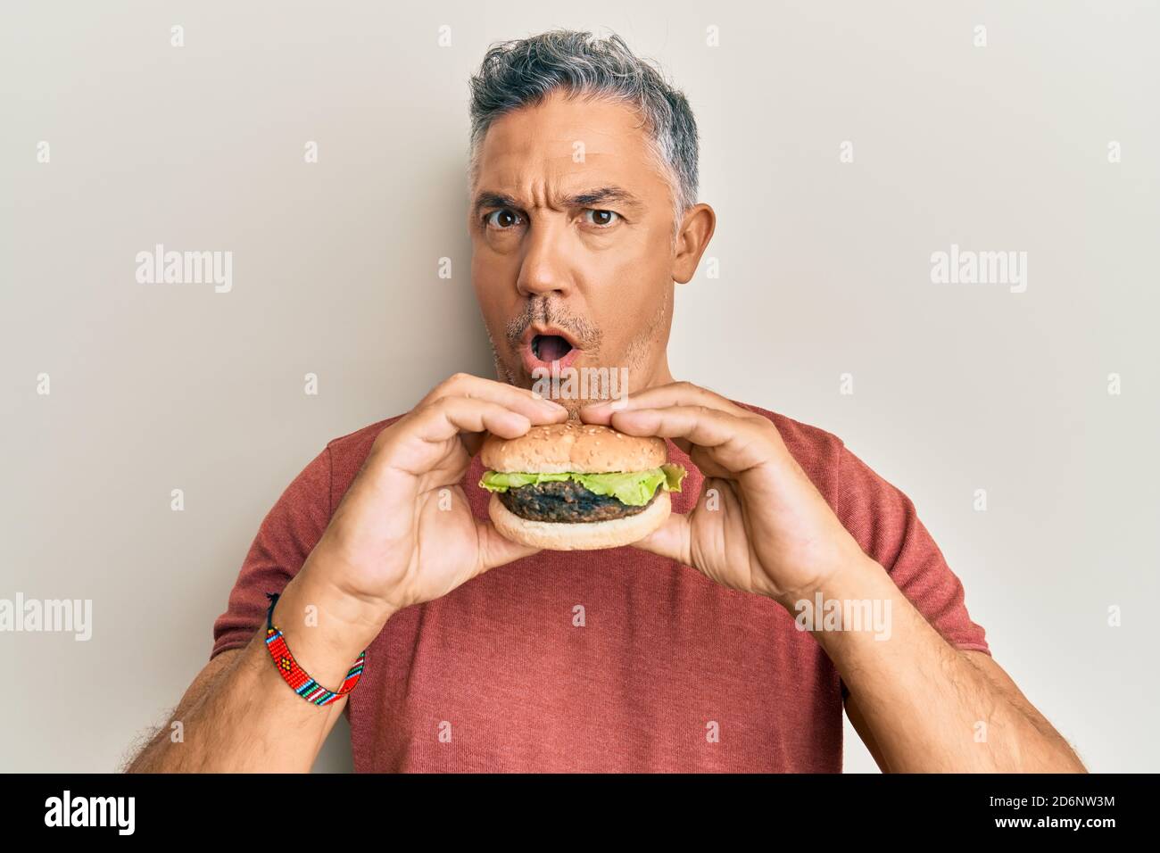 Handsome middle age mature man eating a tasty classic burger in shock ...