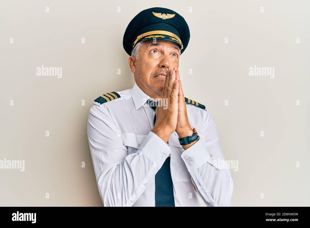 Handsome middle age mature man wearing airplane pilot uniform begging ...