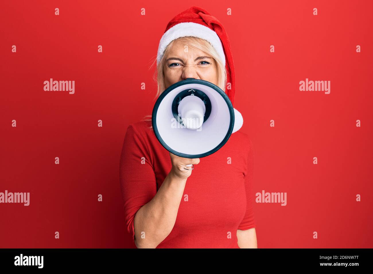 Young blonde woman wearing christmas hat screaming using megaphone over ...