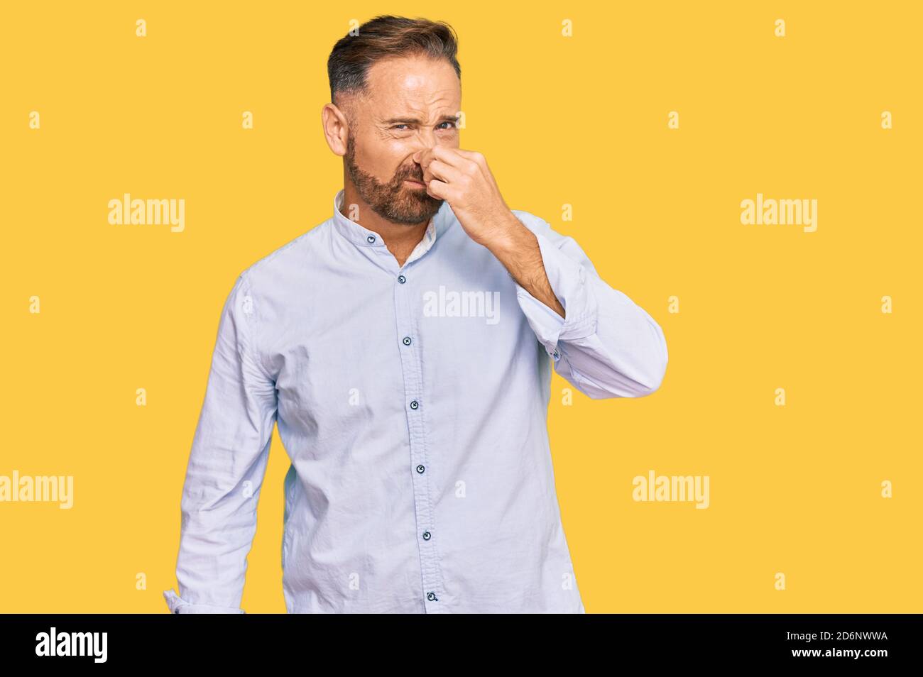 Handsome middle age man wearing business shirt smelling something ...