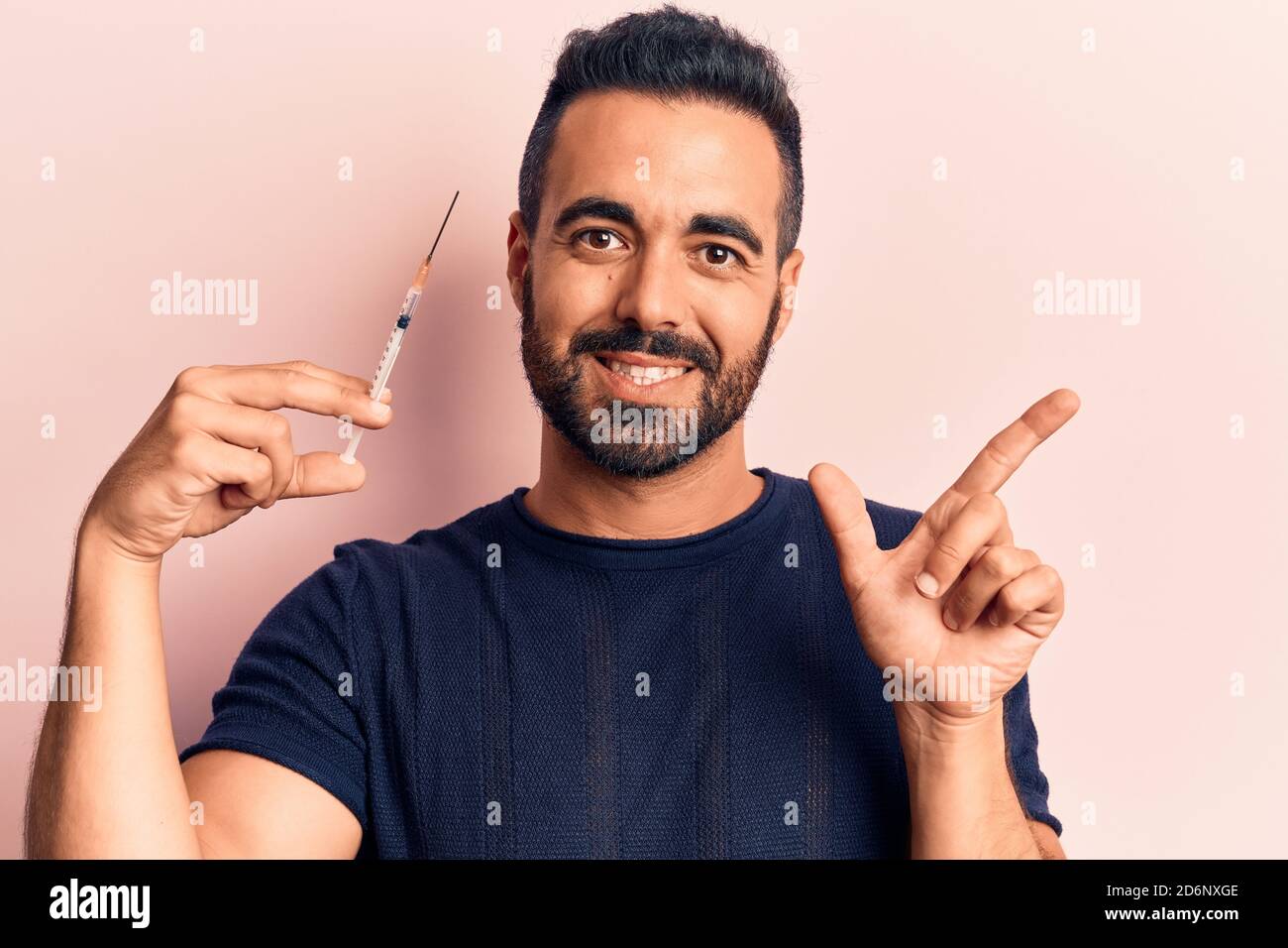 Young hispanic man holding syringe smiling happy pointing with hand and finger to the side Stock ...