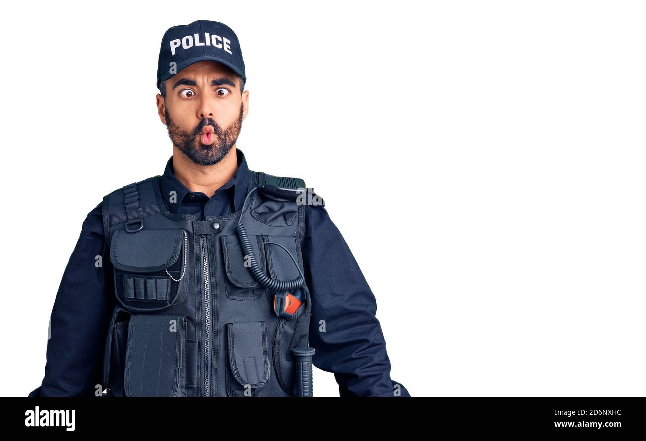 Young hispanic man wearing police uniform making fish face with lips ...