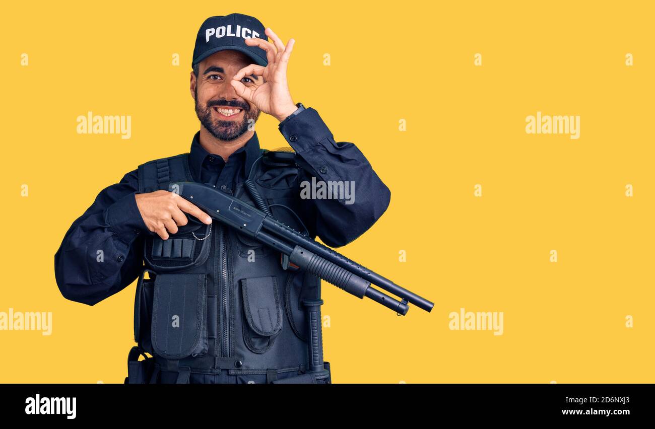 Young hispanic man wearing police uniform holding shotgun smiling happy ...