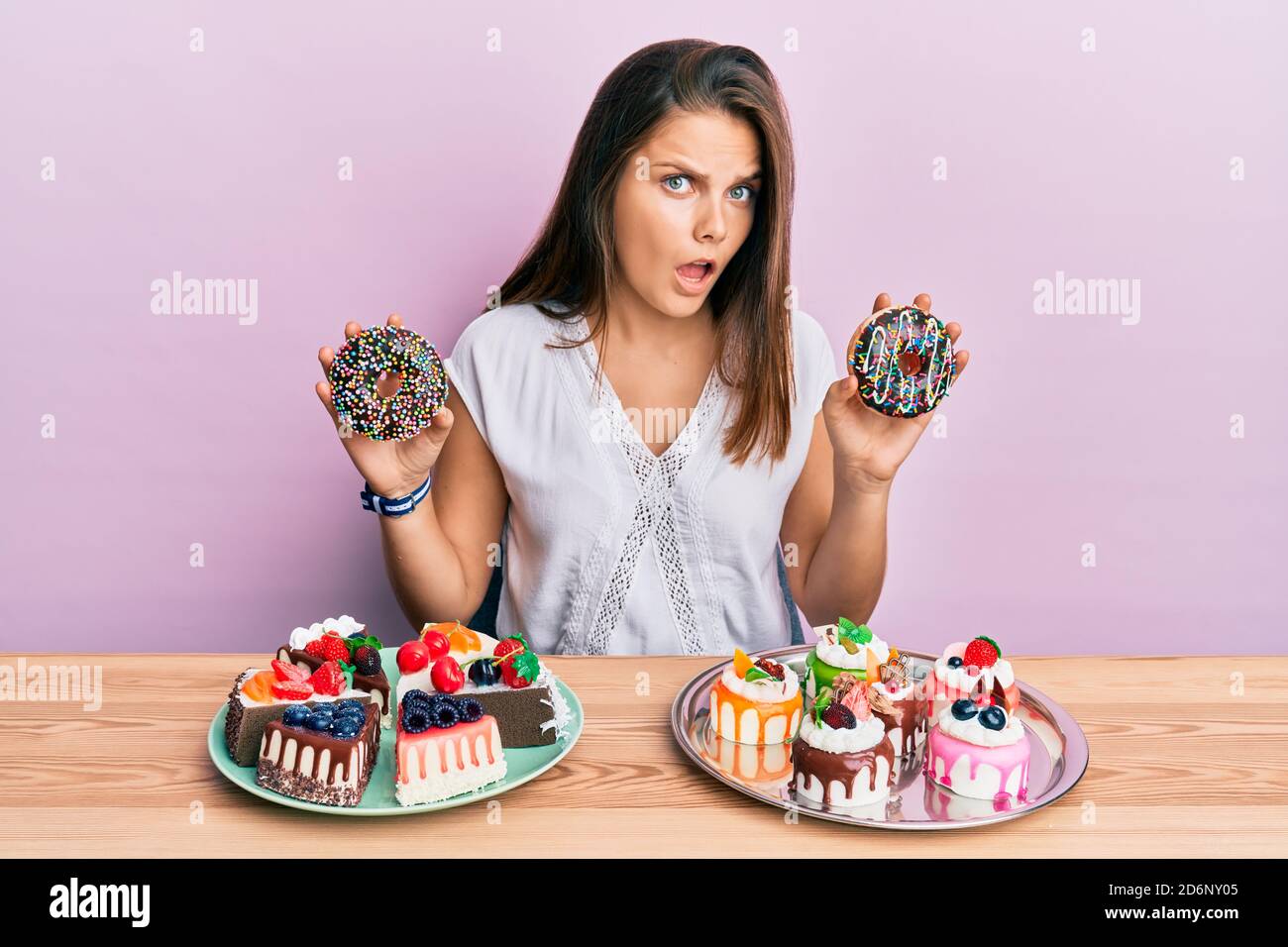 Young caucasian woman eating pastries for breakfast in shock face ...
