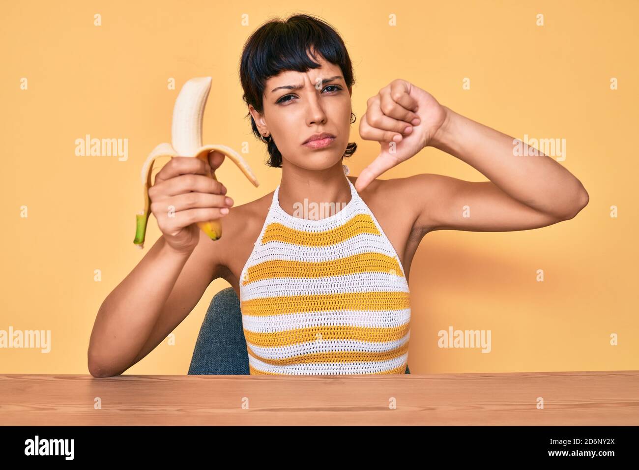 Brunette teenager girl eating banana as healthy snack with angry face ...