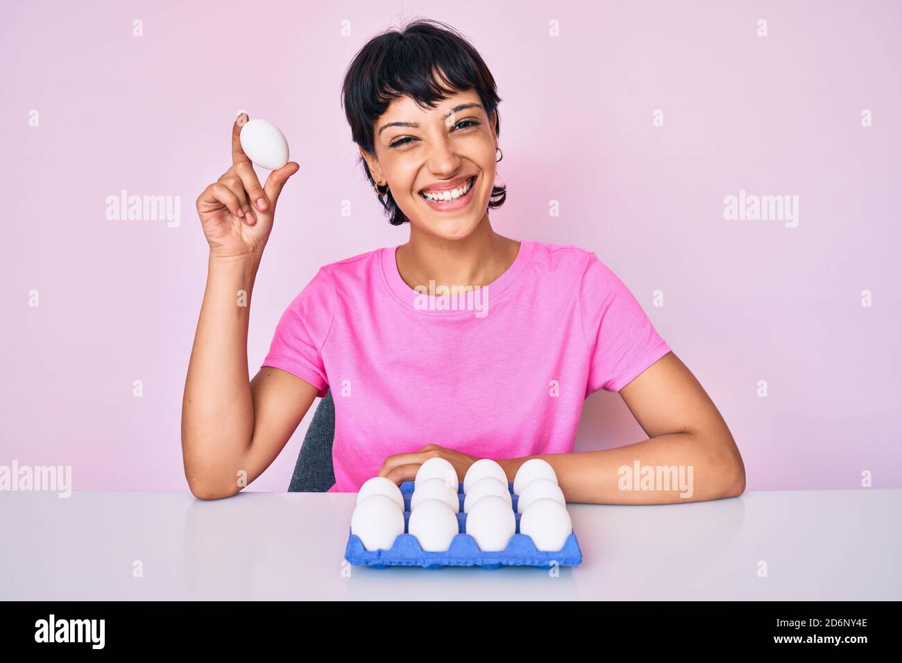Beautiful brunettte woman showing fresh white eggs looking positive and ...