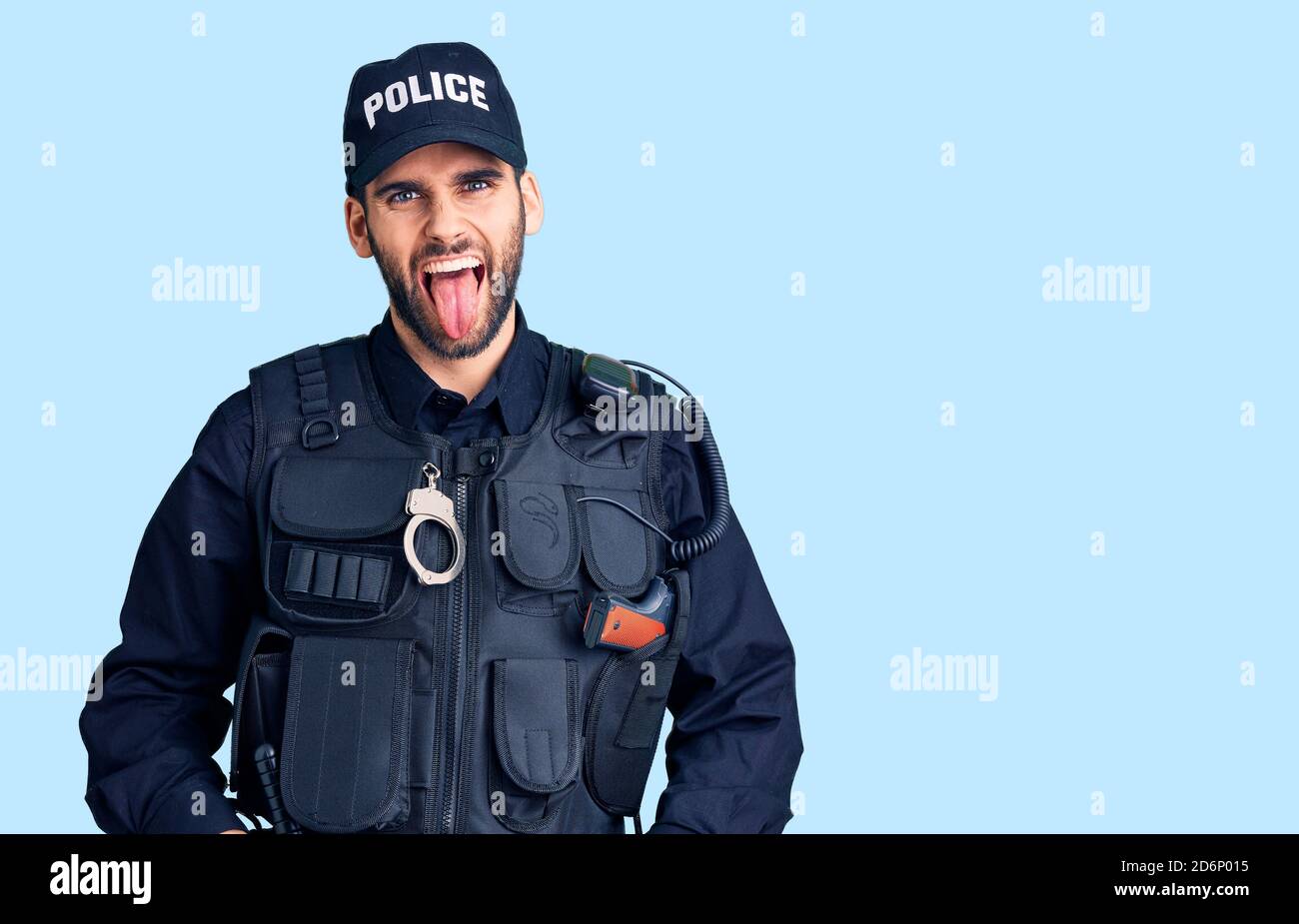 Young handsome man with beard wearing police uniform sticking tongue ...