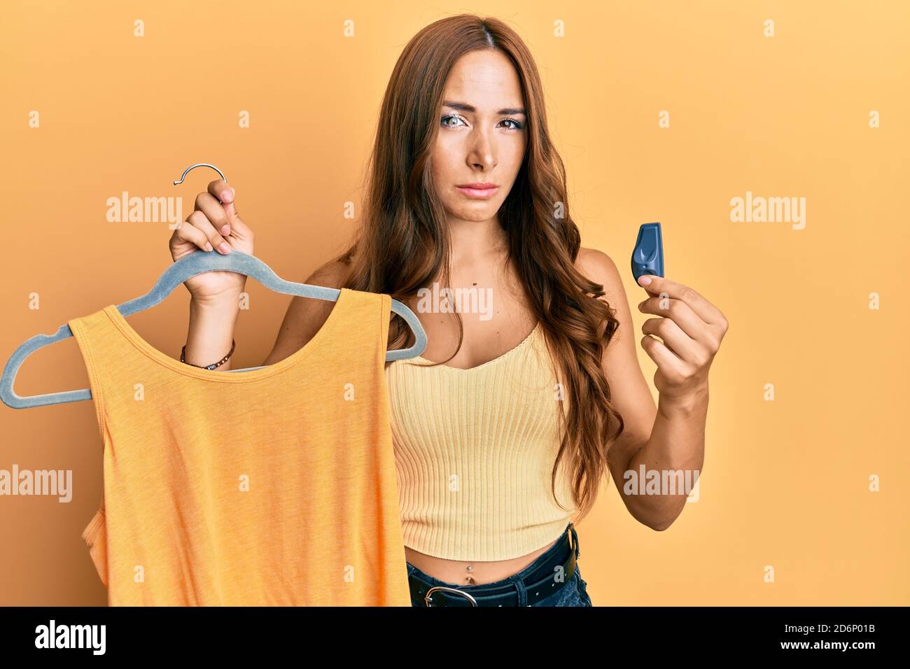 Young brunette shopkeeper woman holding clothes and security alarm ...