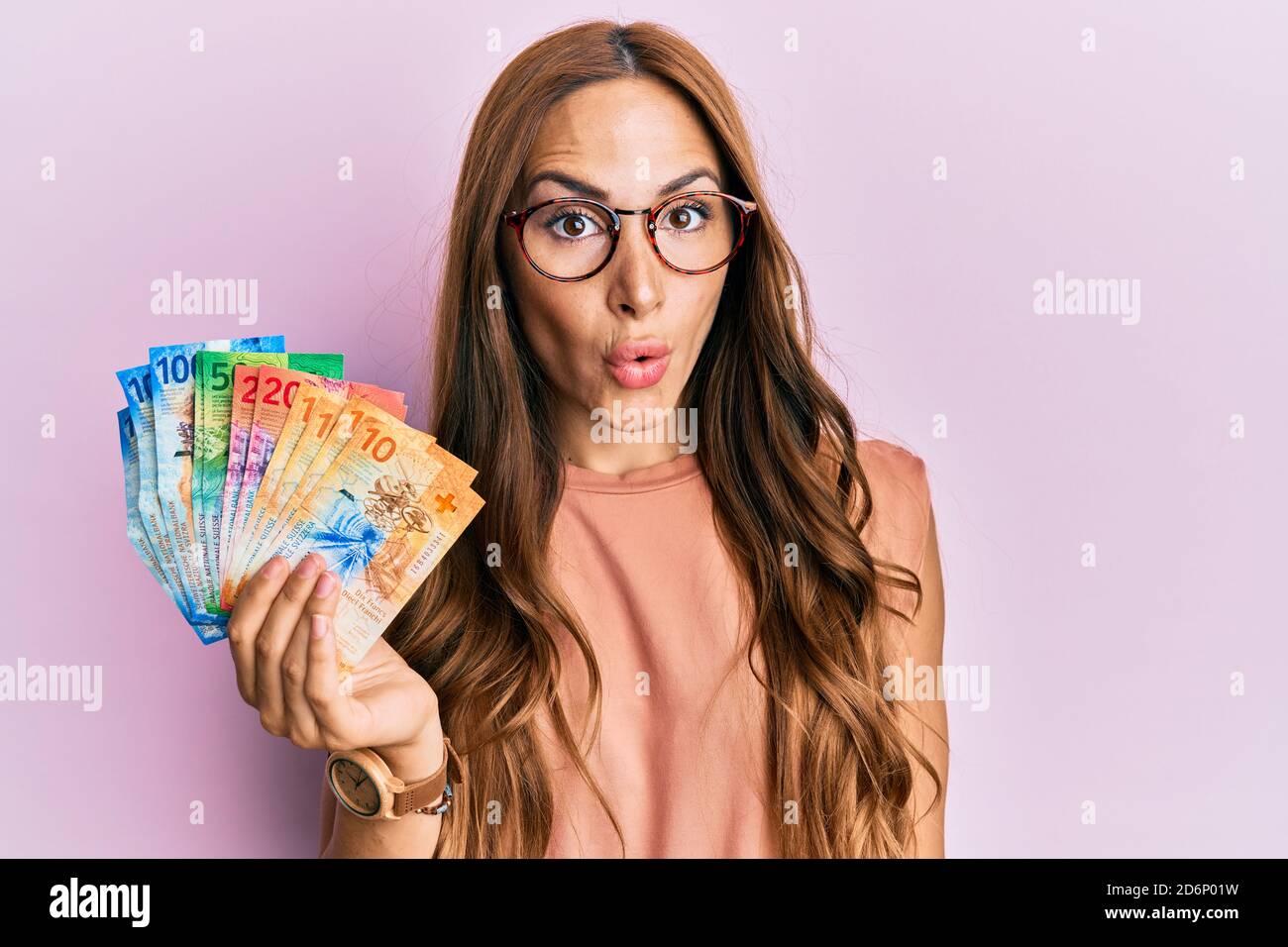 Young brunette woman holding swiss franc banknotes scared and amazed ...