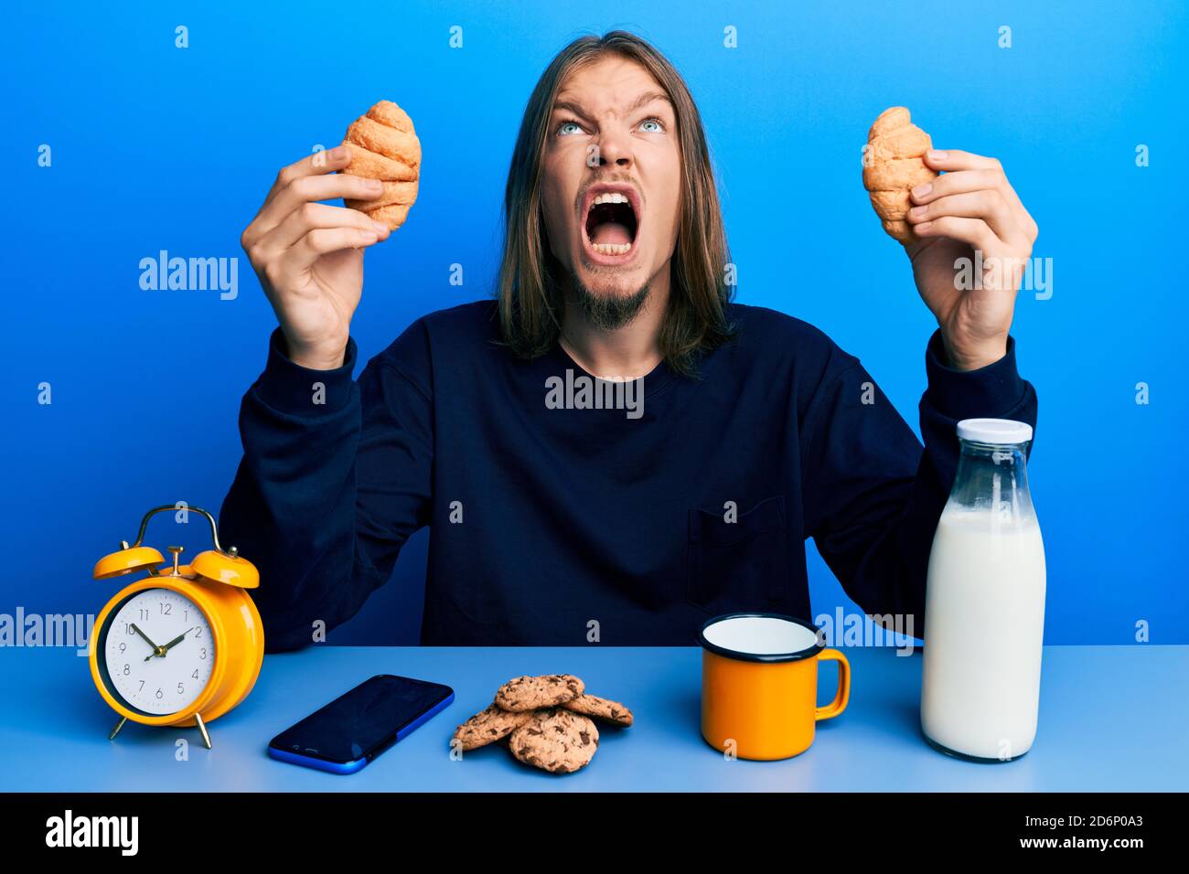 Handsome caucasian man with long hair eating croissant for breakfast ...