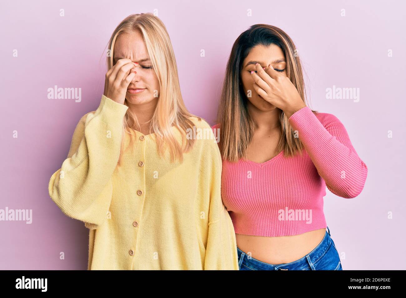 Two friends standing together over pink background tired rubbing nose ...