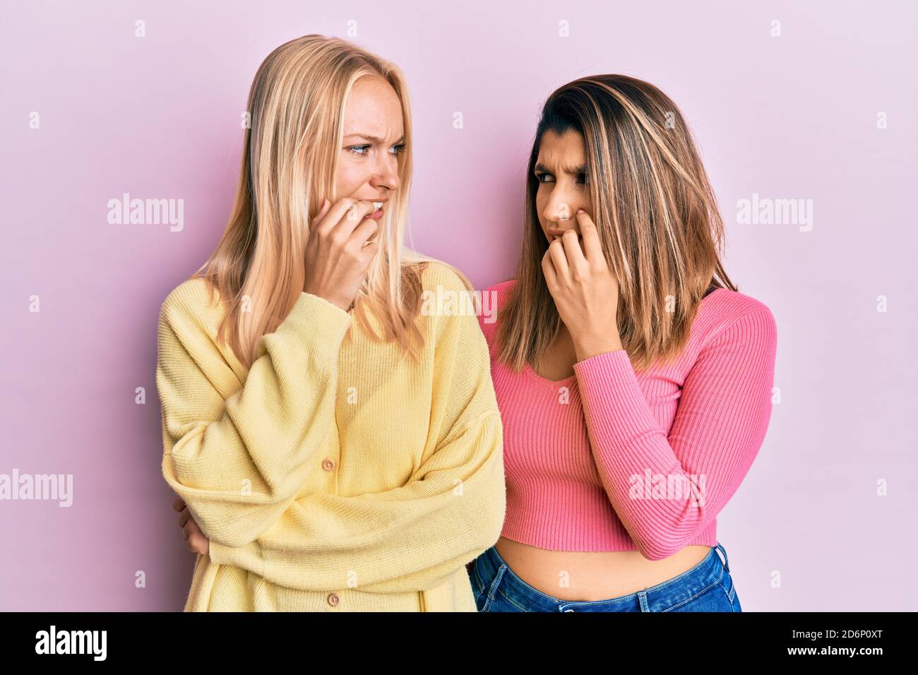 Two friends standing together over pink background looking stressed and ...
