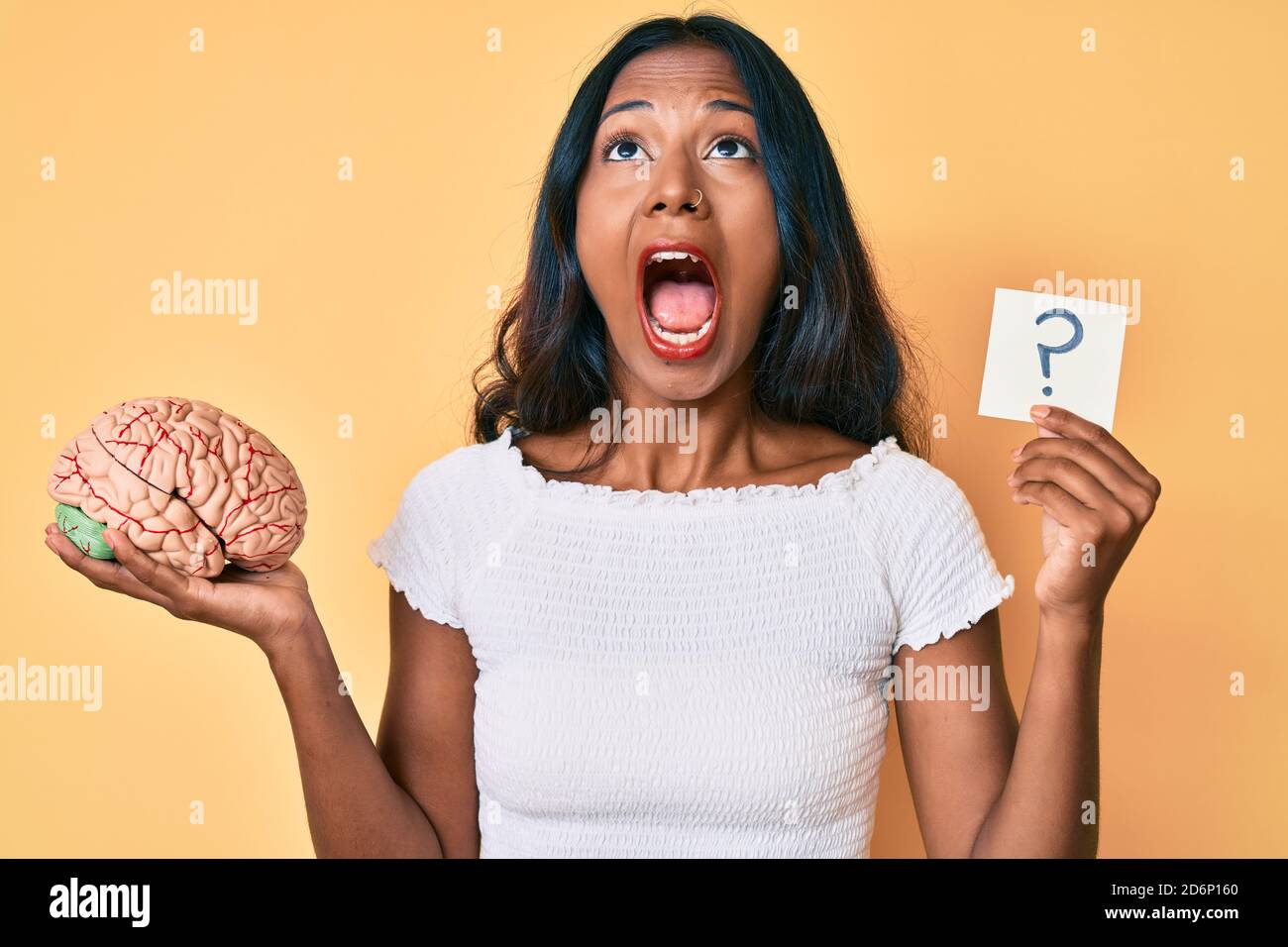 Young indian girl holding brain and question mark reminder angry and ...