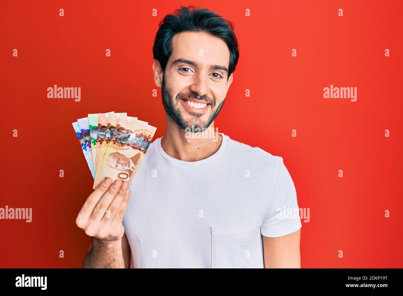 Young hispanic man holding canadian dollars looking positive and happy ...