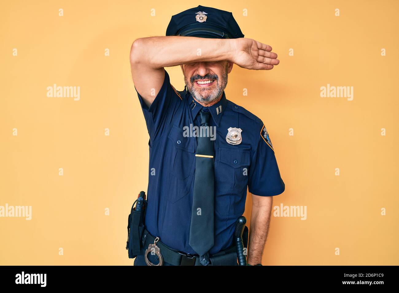 Middle age hispanic man wearing police uniform covering eyes with arm ...