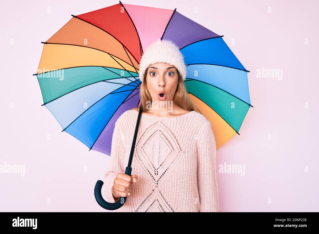 Young brunette woman under colorful umbrella scared and amazed with ...