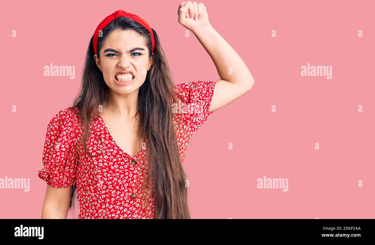 Brunette teenager girl wearing summer dress angry and mad raising fist ...