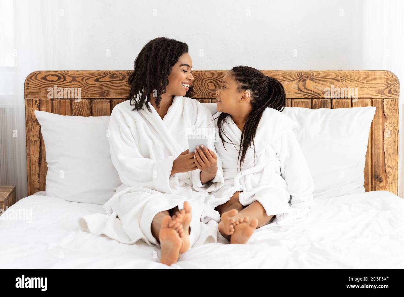 African Mom And Daughter Using Smartphone While Relaxing On Bed In Bathrobes Stock Photo - Alamy