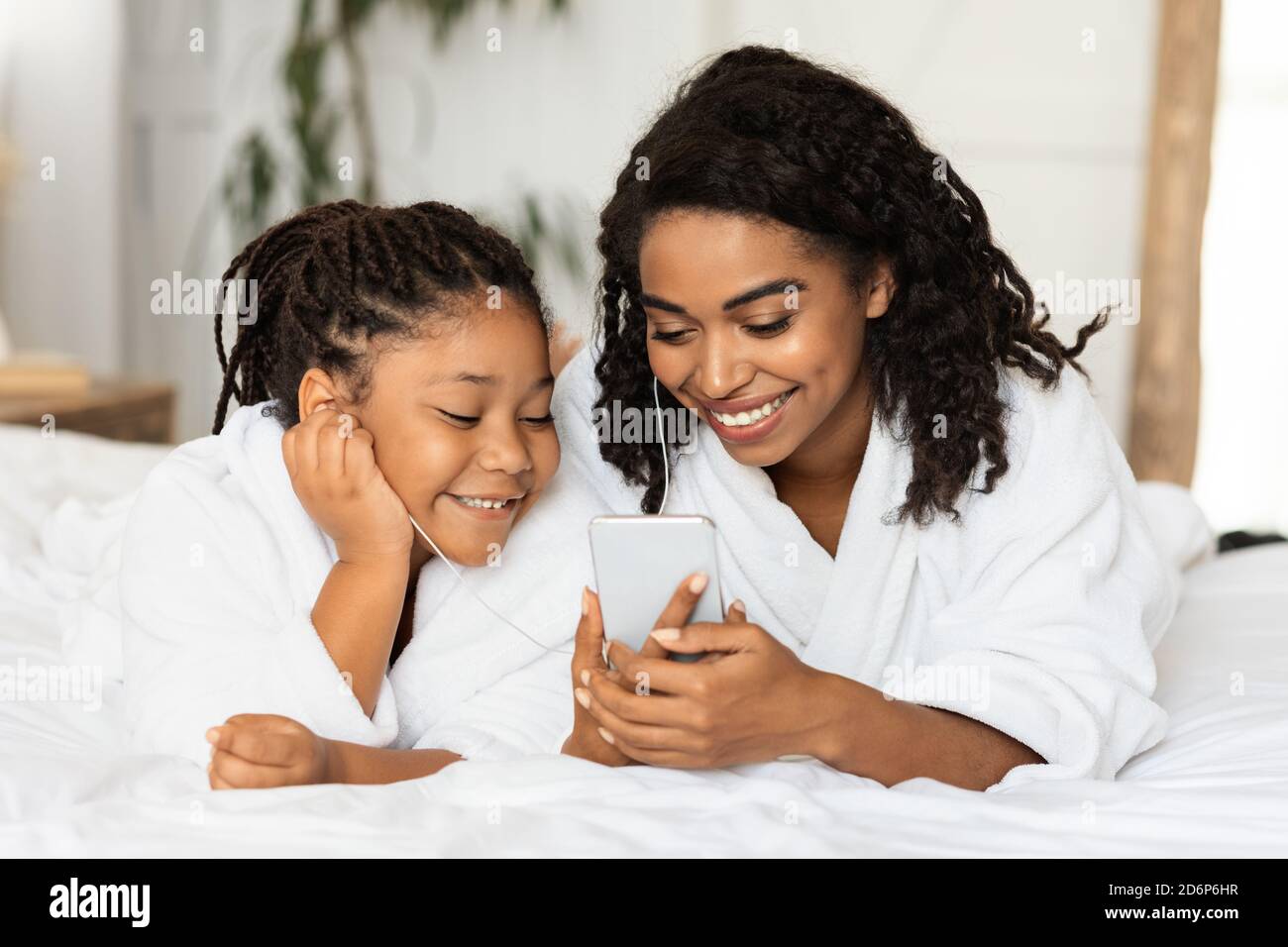 Little black girl and her mom listening music on smartphone, wearing bathrobes Stock Photo - Alamy