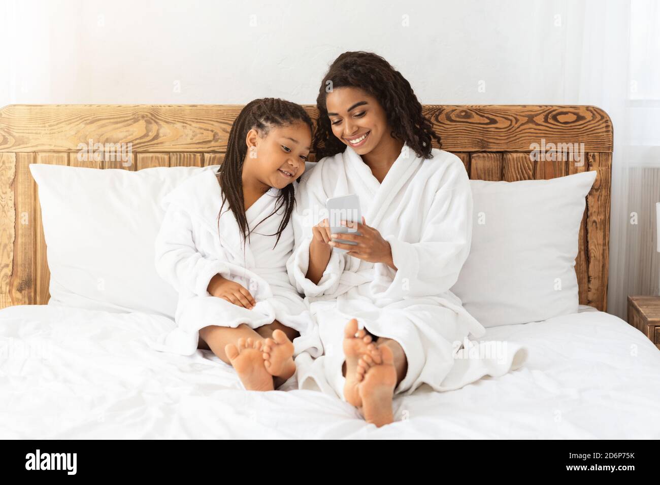 Black Mother And Little Daughter In Bathrobes Resting On Bed With Smartphone Stock Photo - Alamy