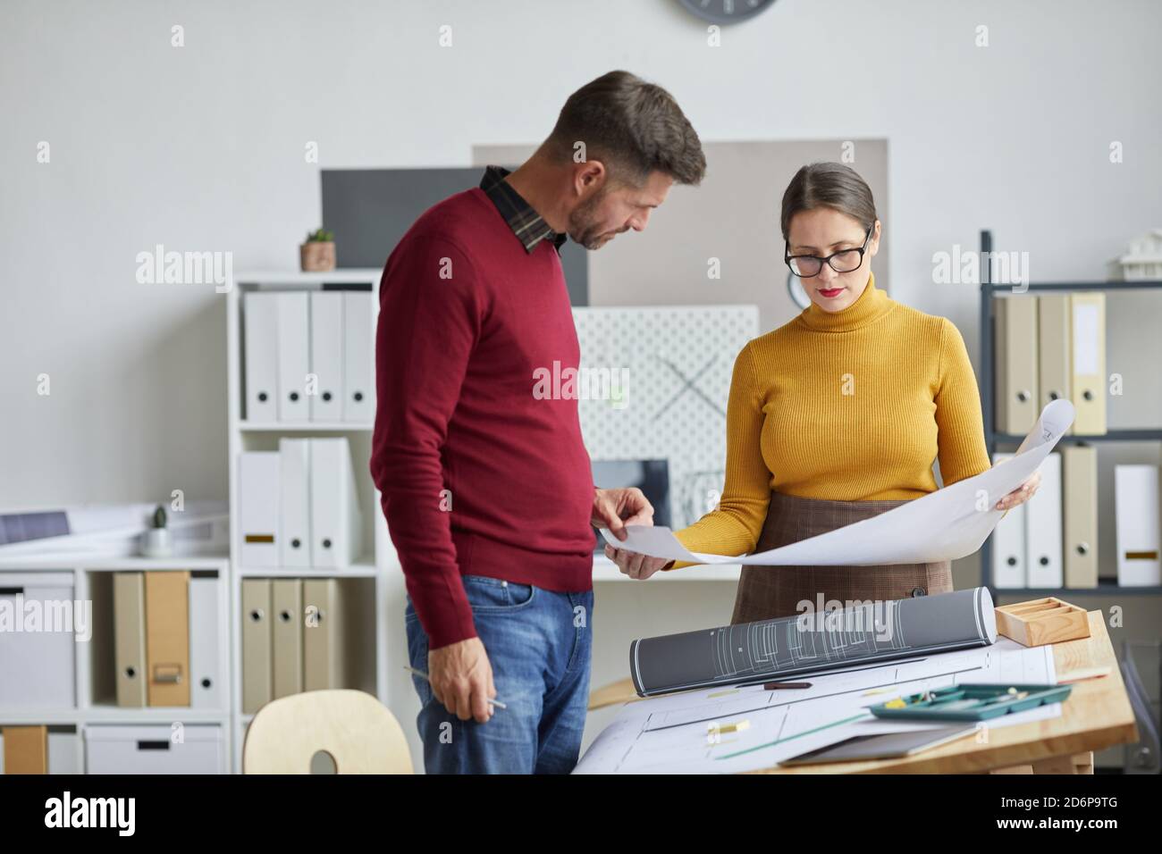 Portrait of two mature architects man and woman working on blueprints ...