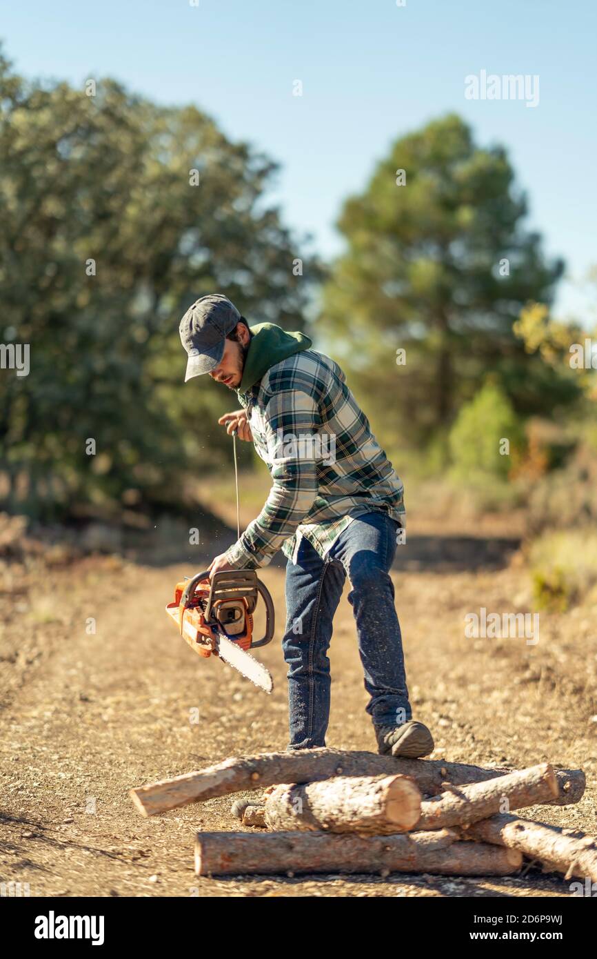 Vertical shot of a young Caucasian man cutting a tree trunk with a ...