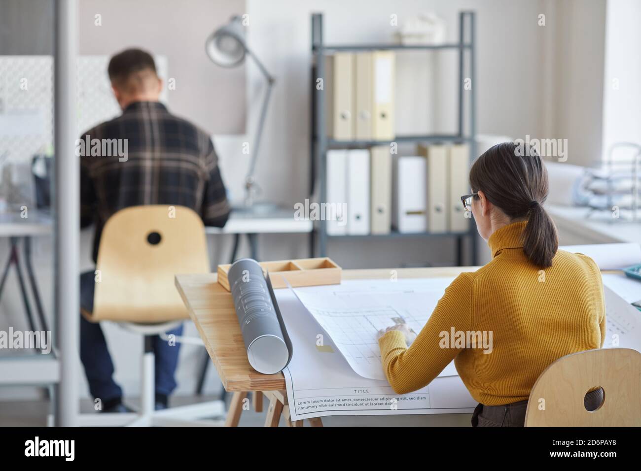 Back view portrait of female architect drawing blueprints while sitting ...