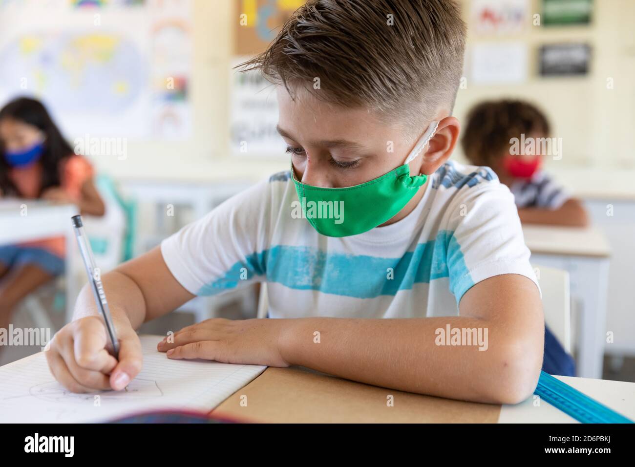 Boy wearing face mask writing while sitting on his desk at school Stock ...