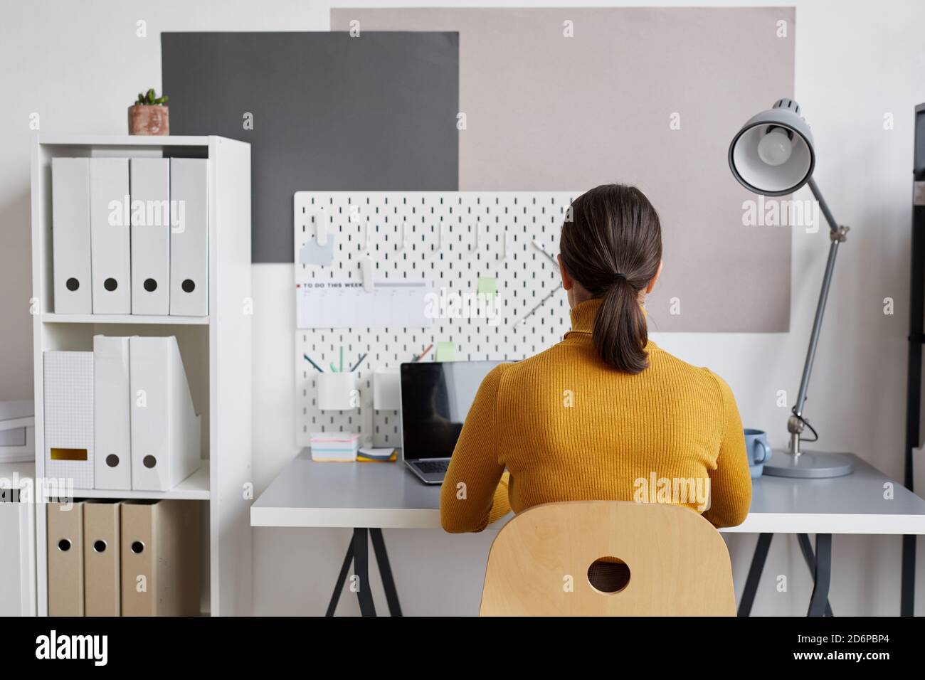 Back view portrait of adult woman using laptop while working at desk at ...