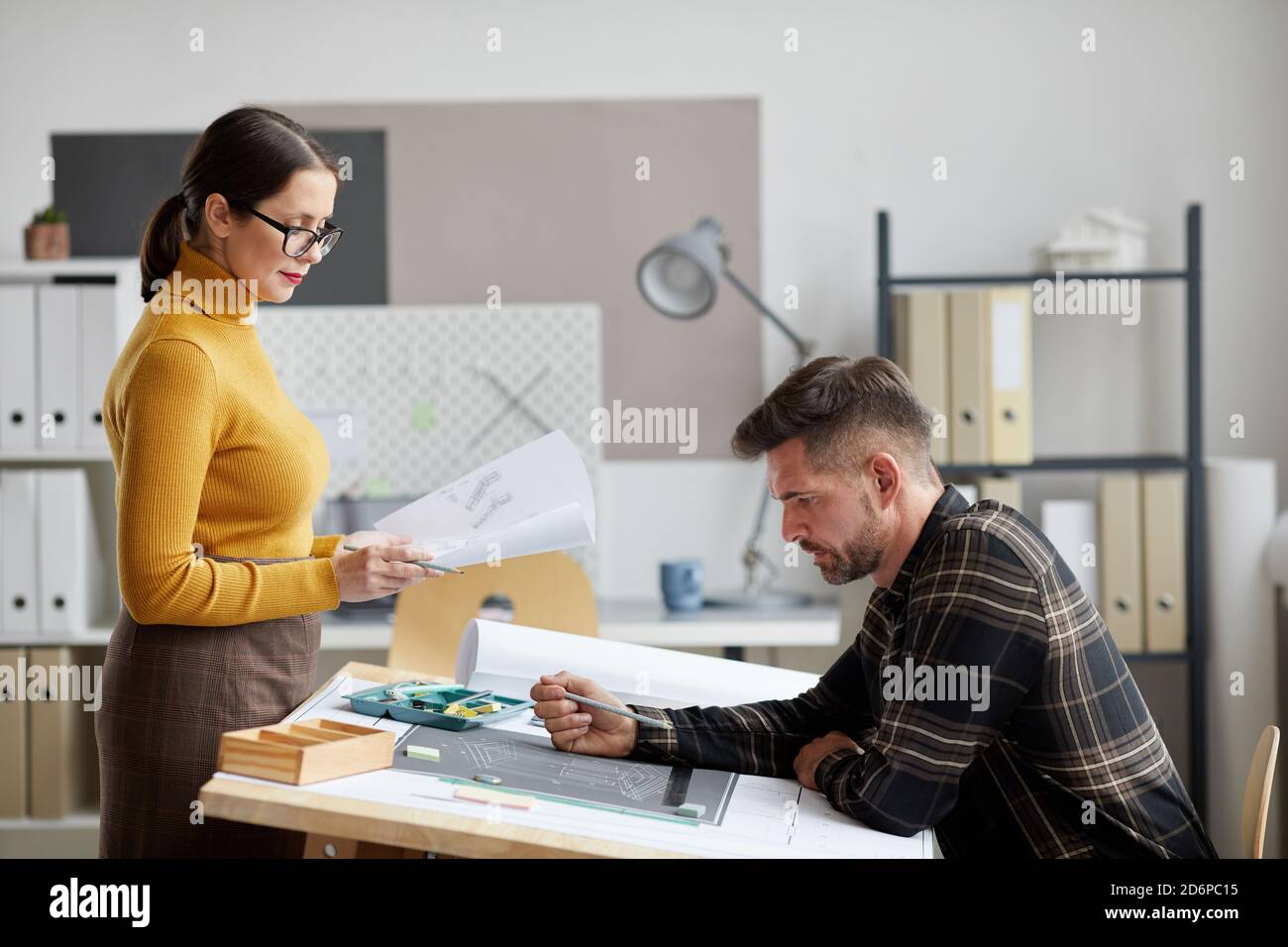 Side view portrait of two adult architects discussing blueprints while ...