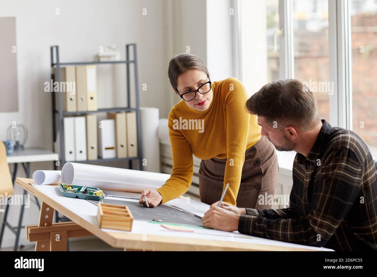 Portrait of two architects pointing at floor plan while working on ...