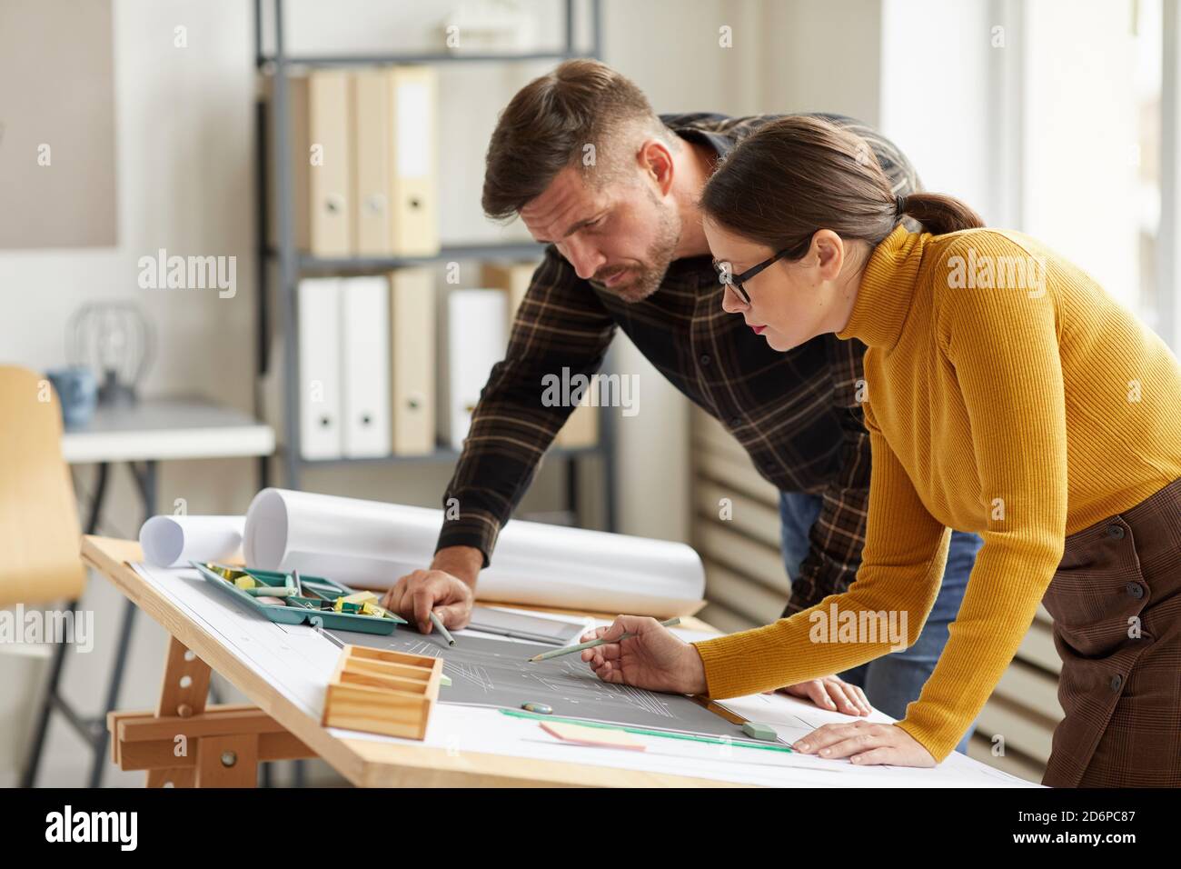 Side view portrait of two architects pointing at floor plan while ...