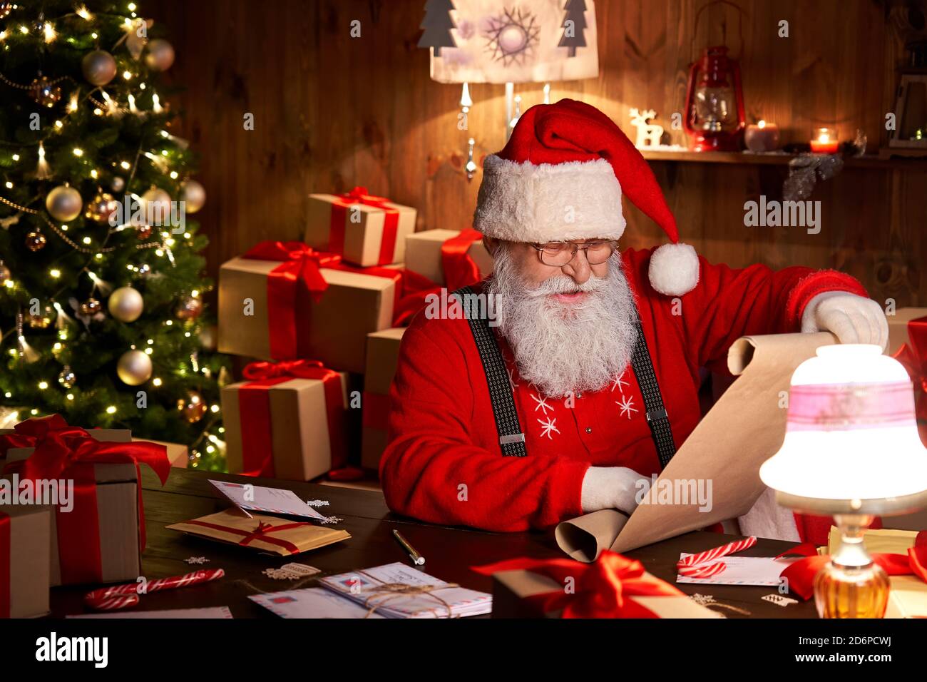 Happy Santa Claus wearing costume reading wish list late on Xmas eve ...