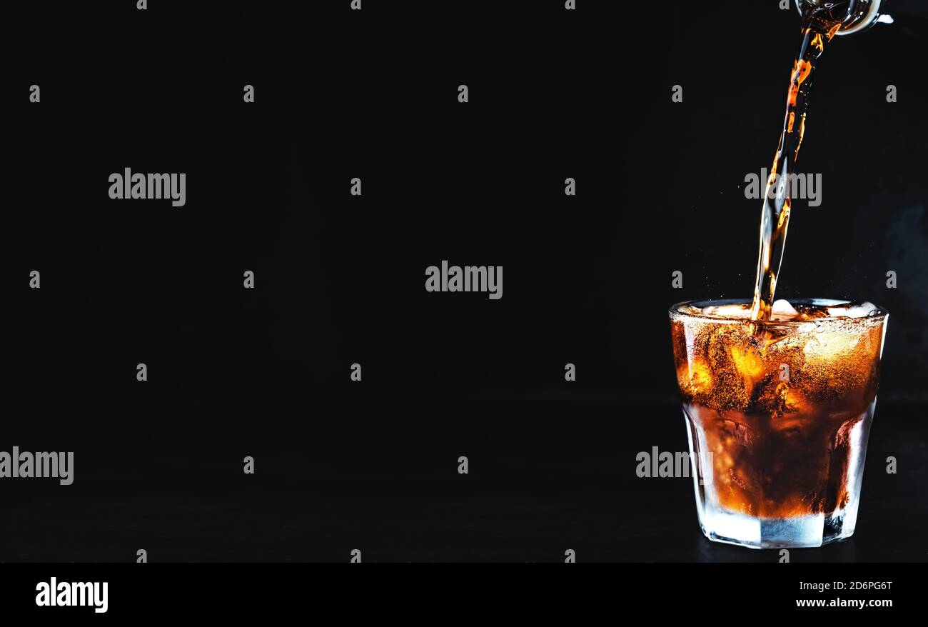 Cool, soft carbonated cola drink is poured into a glass of ice. Soda water refreshing drink ...