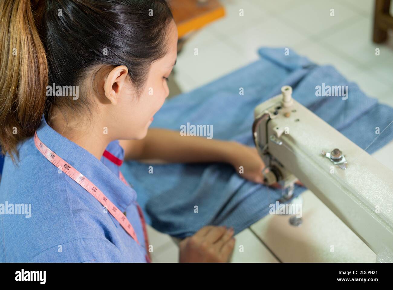 side view of a woman tailor smiles while working on a sewing machine in ...