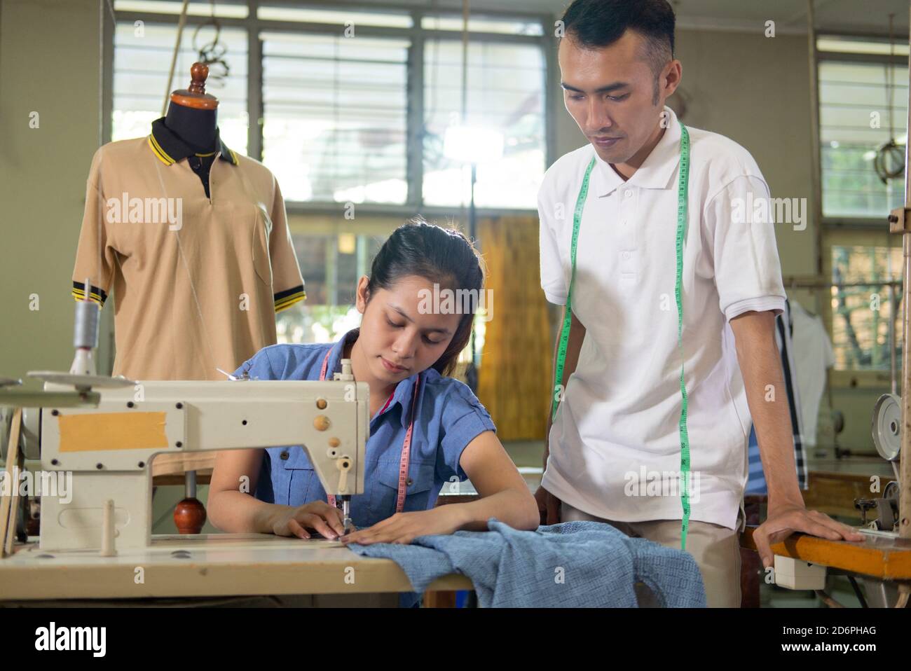 male tailor stands beside and sees the female tailor using the sewing ...
