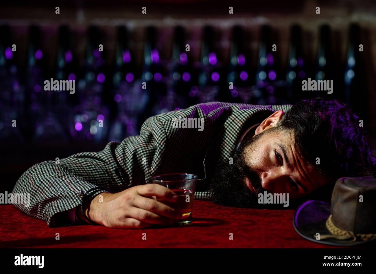 Upset bearded man drinker alcoholic sitting at bar counter with glass drinking whiskey alone ...