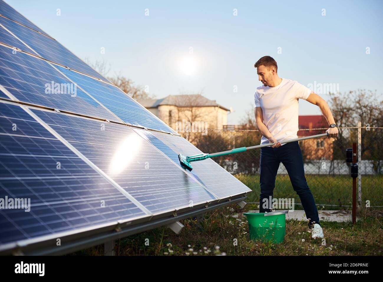 Young man is cleaning a solar panel with a mop, pv plant in rural area ...
